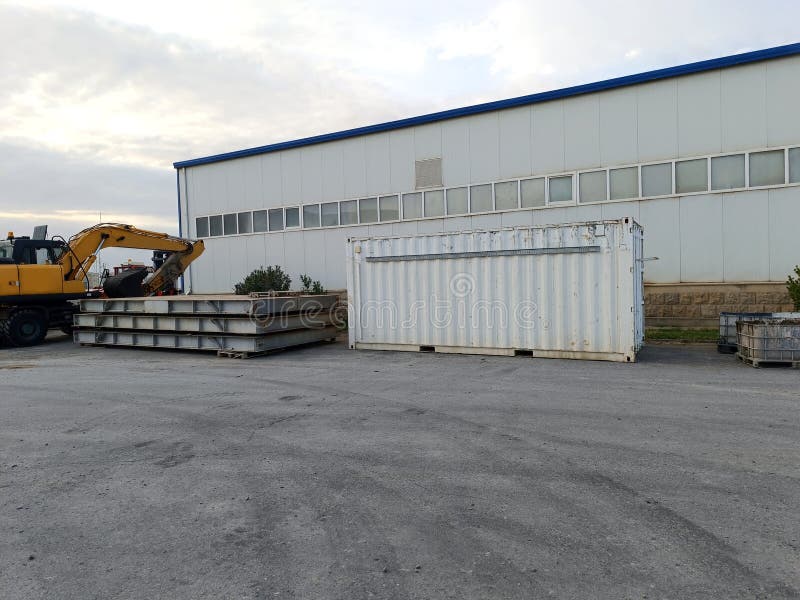 An Excavator on a Break Near a Warehouse, Next To a Container Stock ...