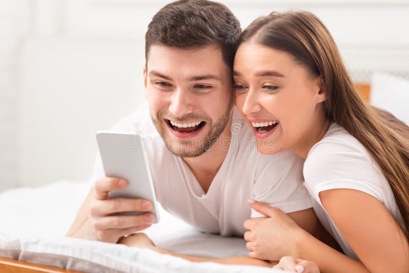 Excited Couple Using Cellphone Texting Lying in Bed at Home Stock Image ...