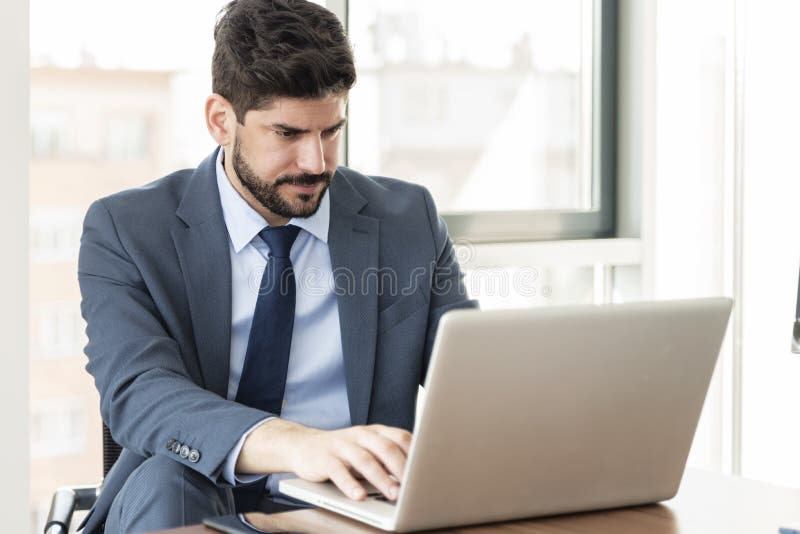 Executive Businessman Sitting at Office Desk and Using Laptop while ...