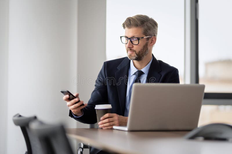 Executive Businessman Text Messaging and Using Laptop at Office Desk ...