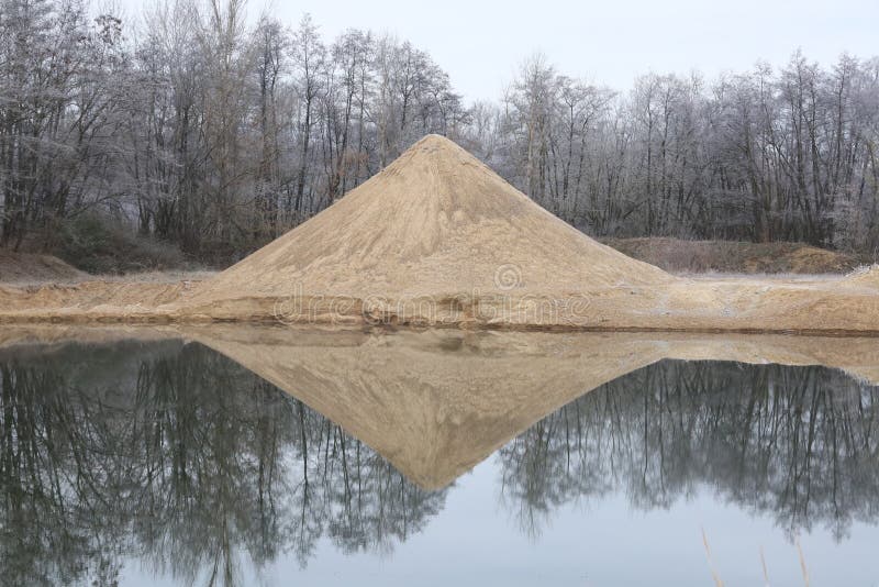 Eye-level Shot of a Pile of Sand Reflecting in a Lake Surrounded by ...