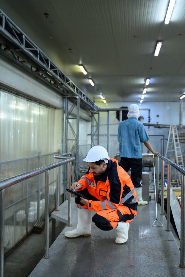 Factory Worker in Protective Uniform Using Digital Tablet To Inspect Industrial Equipment Inside ...