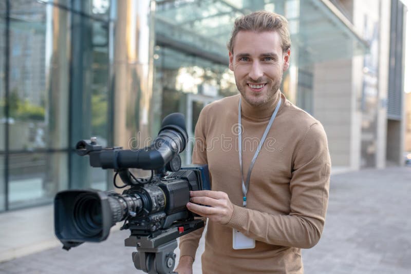 Smiling Fair-haired Cameraman Carring Camera with Tripod Outside Stock ...