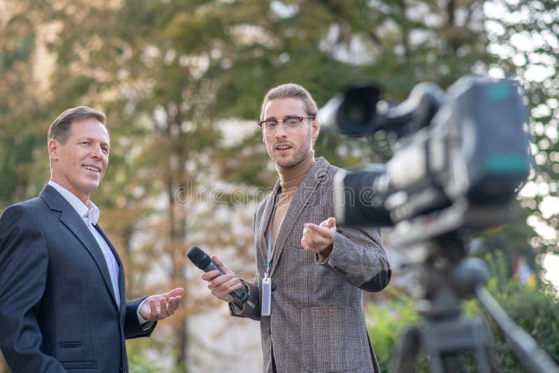 Fair-haired Male Journalist Interviewing Smiling Mature Male in Front ...
