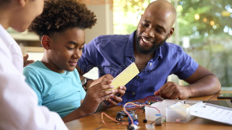Family Around Table at Home Using Laptop with Parents Helping Son with ...
