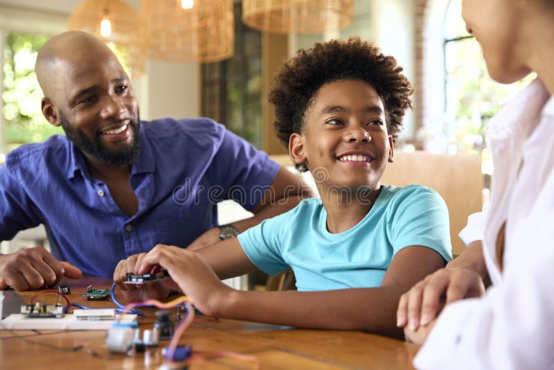 Family Around Table at Home Using Laptop with Parents Helping Son with ...