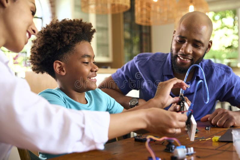 Family Around Table at Home Using Laptop with Parents Helping Son with ...