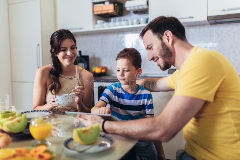 Family Eating Breakfast at Kitchen Table and Using Digital Tablet Stock ...