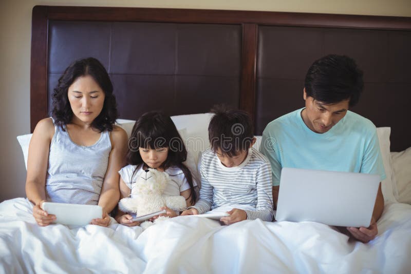 Family Using Digital Tablet, Mobile Phone and Laptop on Bed in the Bed ...