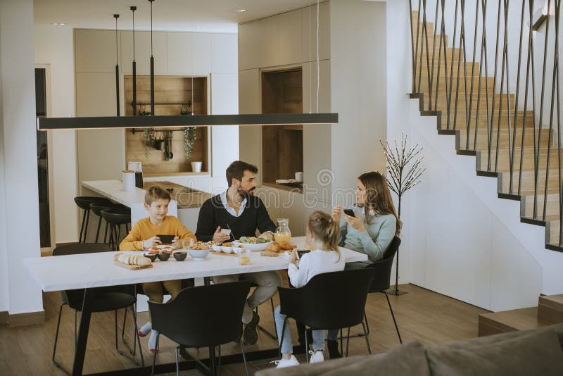 Family Using Mobile Phones while Having Breakfast at Dining Table at ...