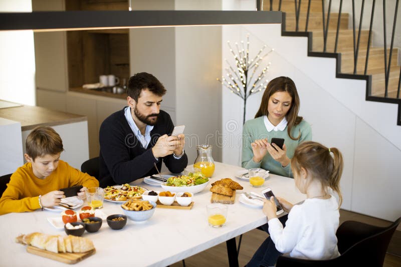 Family Using Mobile Phones while Having Breakfast at Dining Table at ...