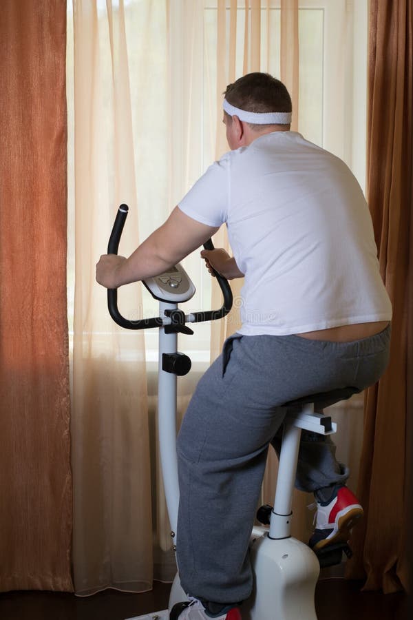 Fat Guy Exercising on Stationary Training Bicycle and Drinking Water ...