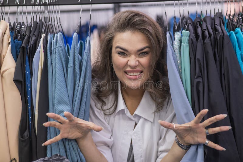 A Fat Woman in a Plus Size Store Peeks Out from Behind Racks of Clothes ...
