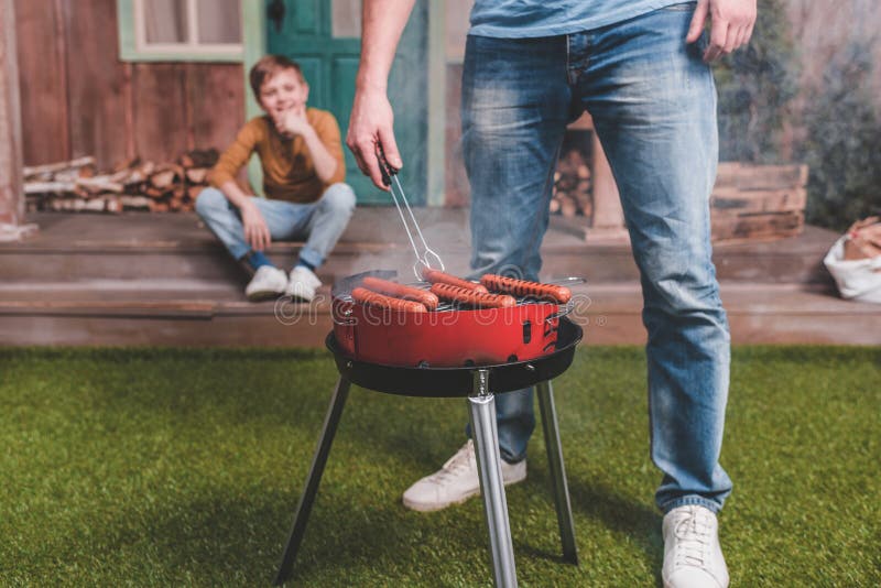 Father Cooking Hot Dog Sausages with Son Behind Stock Image - Image of ...