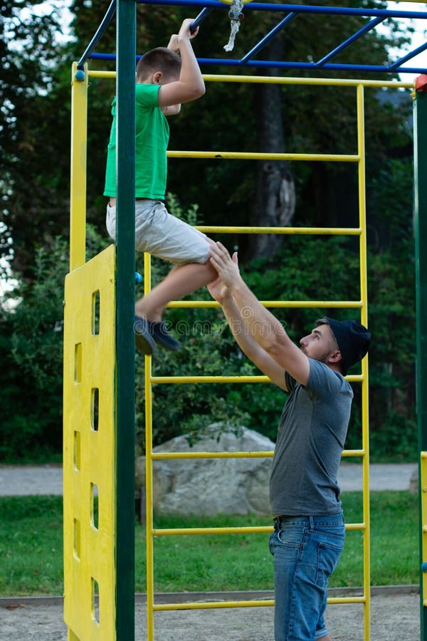 Father Helping His Son Do Pull-ups on a Playground Climbing Frame ...