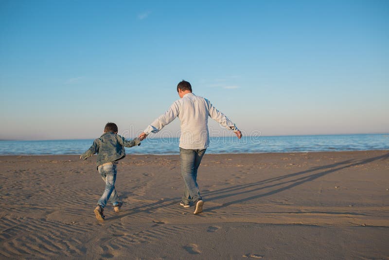 Father and His Little Son Run on a Beach in the Evening. Back View ...