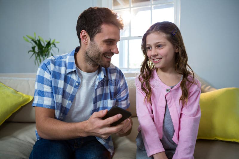 Father Holding Mobile Phone And Interacting Daughter With In The Living