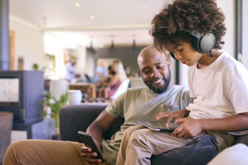 Father with Mobile Phone and Son Using Digital Tablet with Headphones ...
