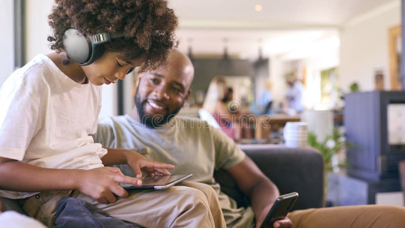 Father with Mobile Phone and Son Using Digital Tablet with Headphones ...
