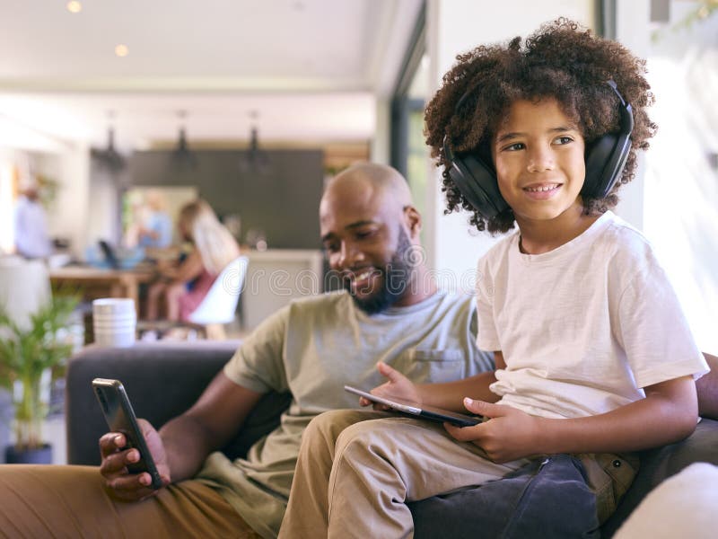 Father with Mobile Phone and Son Using Digital Tablet with Headphones ...
