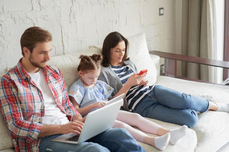 Father, Mother and Daughter Using Electronic Devices Sitting on Sofa at Living Room. Stock Image ...