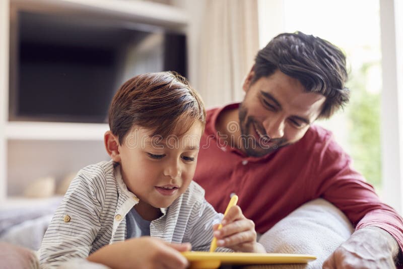 Father and Son at Home on Sofa in Lounge Playing with Digital Tablet or ...