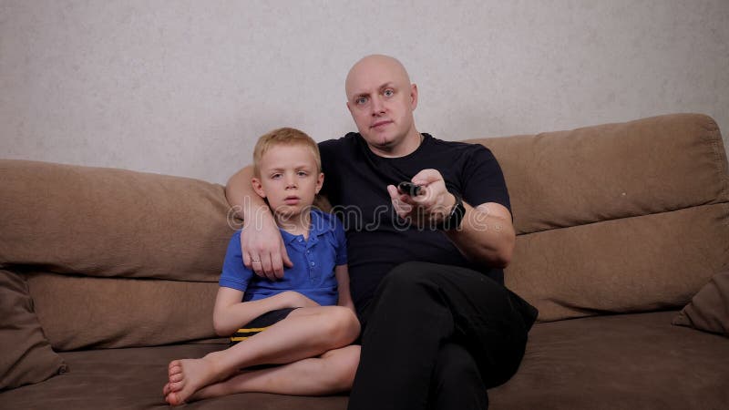 A Father and Son with a Remote Control Watch TV Sitting at Home on the ...