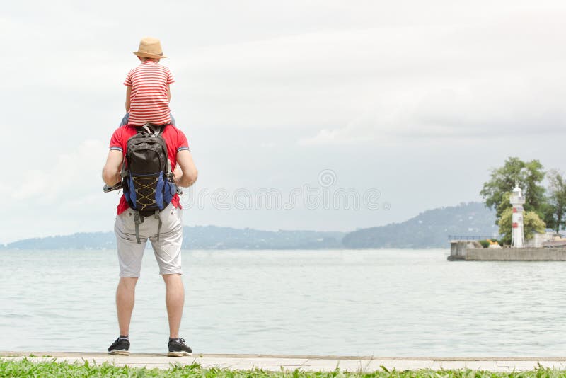 Father and Son on Shoulders Stand on the Pier, Lighthouse and Mountains ...