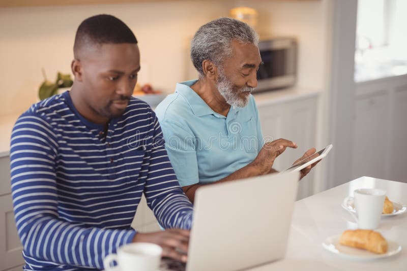 Father and Son Using Laptop and Digital Tablet in Kitchen Stock Image ...