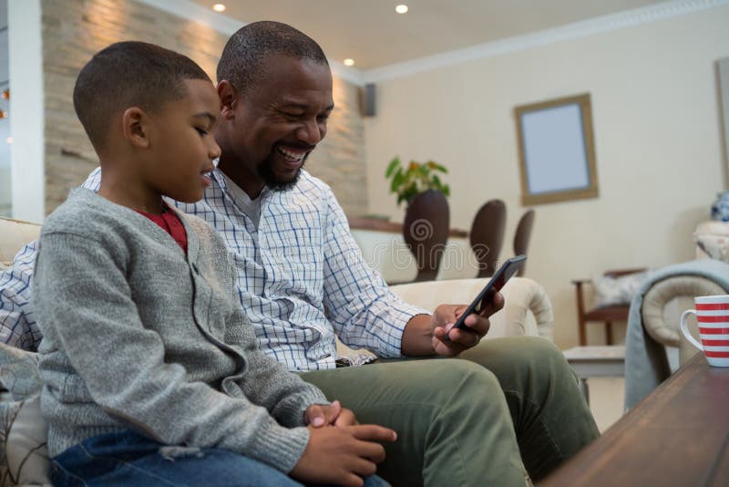 Father and Son Using Mobile Phone on Sofa in Living Room Stock Photo ...