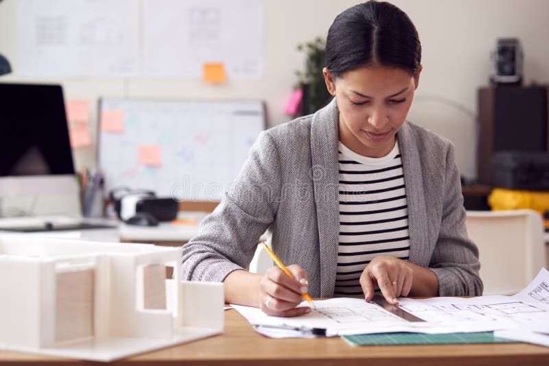 Female Architect Working in Office with Model on Desk Studying Plans ...