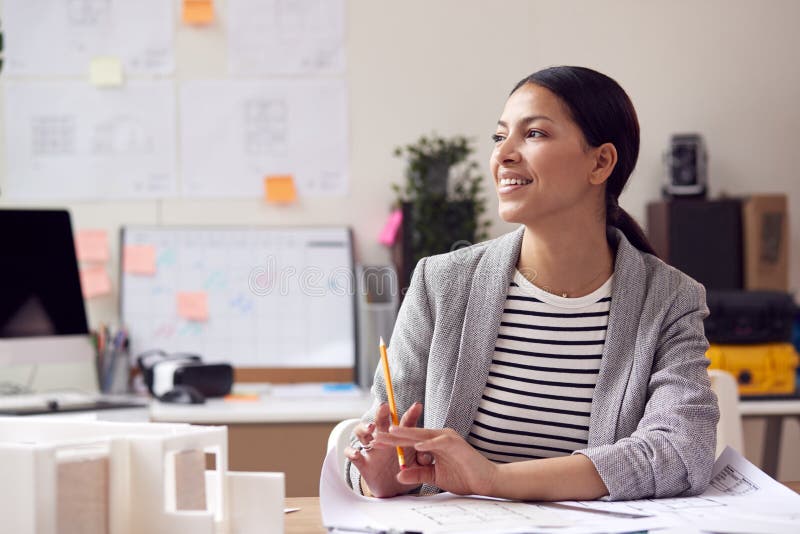 Female Architect Working in Office with Model on Desk Studying Plans ...