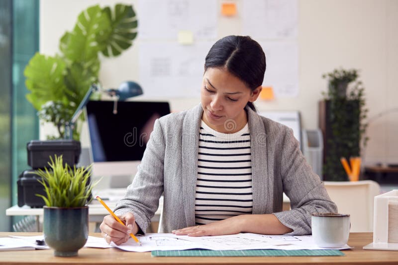 Female Architect Working in Office Sitting at Desk Studying Plans for ...