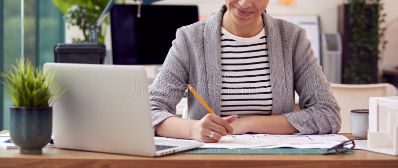 Female Architect Working in Office Sitting at Desk Studying Plans for ...