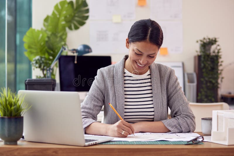 Female Architect Working in Office Sitting at Desk Studying Plans for ...