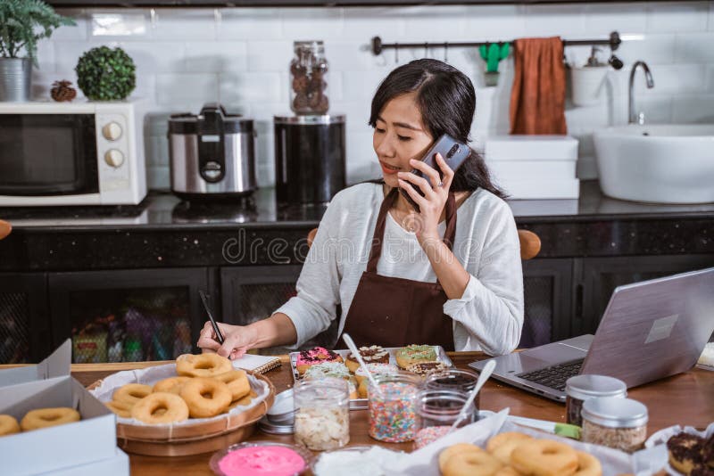 Female Chef in an Apron Takes a Call Using a Cellphone while Writing on ...