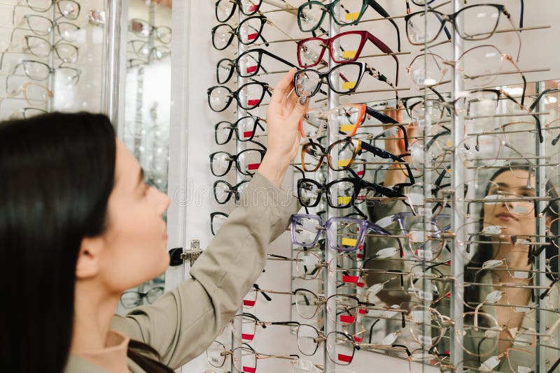 Female Client Chooses Eyeglasses from the Stand in the Optical Store ...