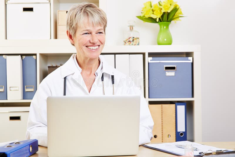 Senior Female Doctor with Stethoscope at Desk & Computer Stock Photo ...