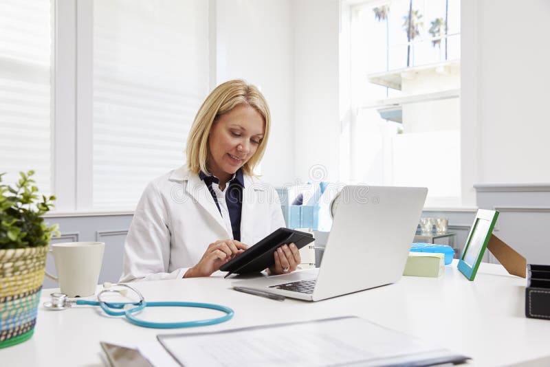 Female Doctor Sitting at Desk Using Digital Tablet in Office Stock ...