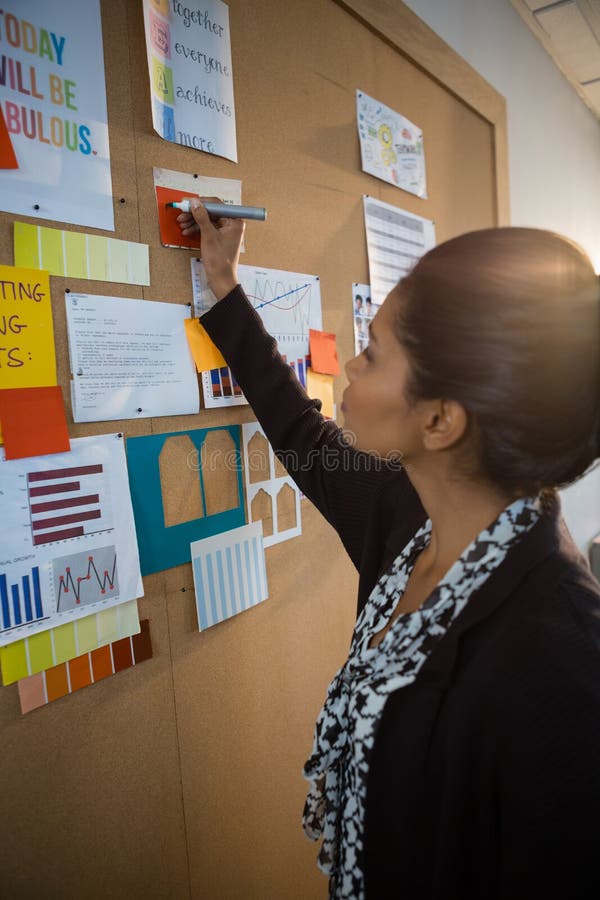 Female Executive Writing on Sticky Note at Bulletin Board Stock Photo ...