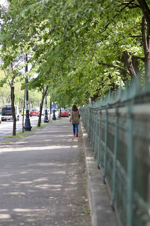 Female Figure Strides Confidently Down a City Sidewalk, Surrounded by a ...