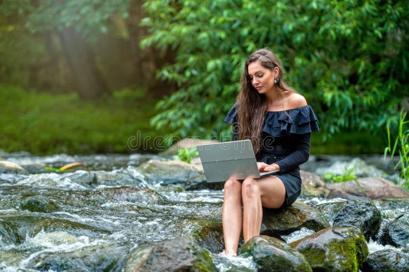 Woman Freelancer Sitting On A Rock In The River And Using A Laptop