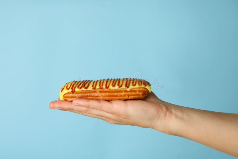 Female Hand Hold Tasty Eclair on Blue Background Stock Photo - Image of ...