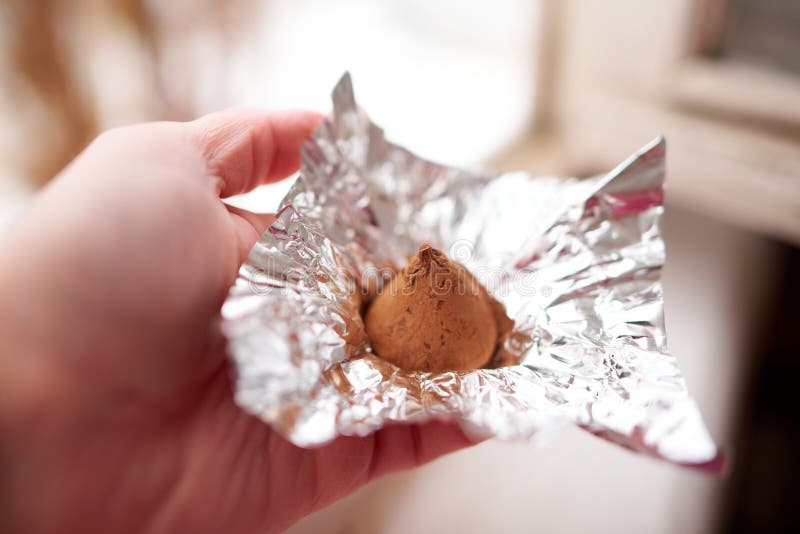 A Female Hand Holds a Chocolate Truffle Candy Wrapped in a Foil Wrapper ...