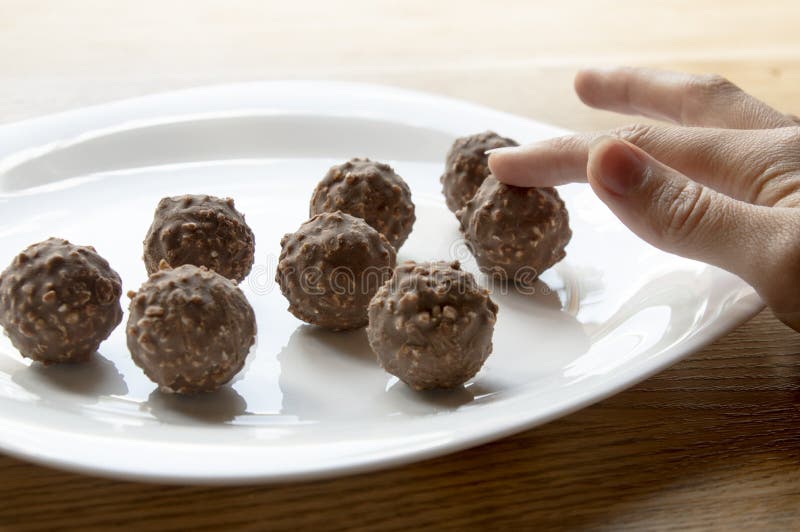 Female Hand Tries Round Chocolate Candy with Nuts on a White Plate ...