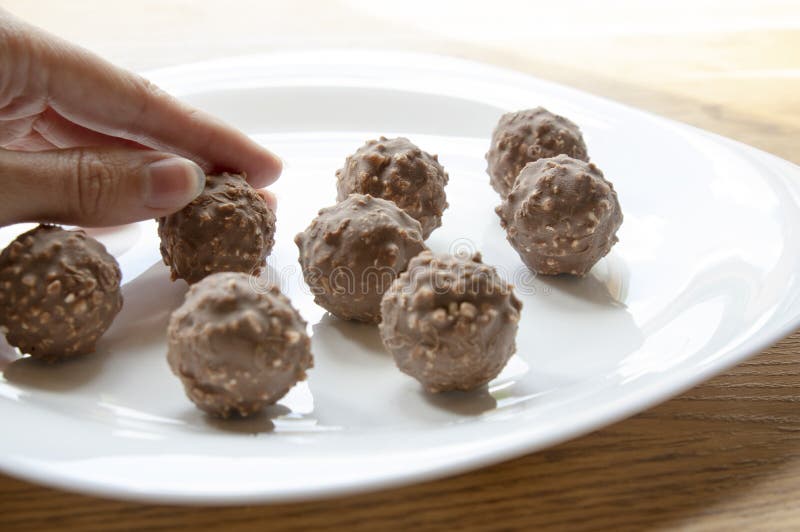 Female Hand Tries Round Chocolate Candy with Nuts on a White Plate ...
