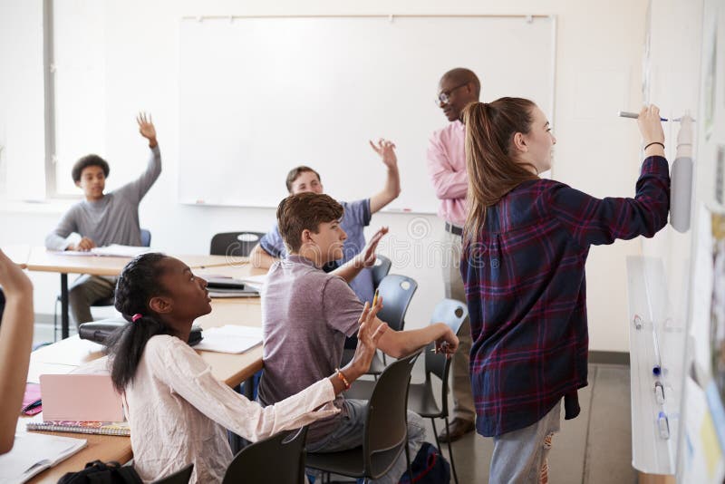 Pupil Writing in Notebook at Desk in Classroom. Girl Raising Hand in ...