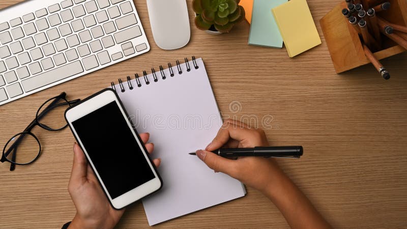 Female Holding Mobile Phone and Making Note on Notebook. Stock Image ...