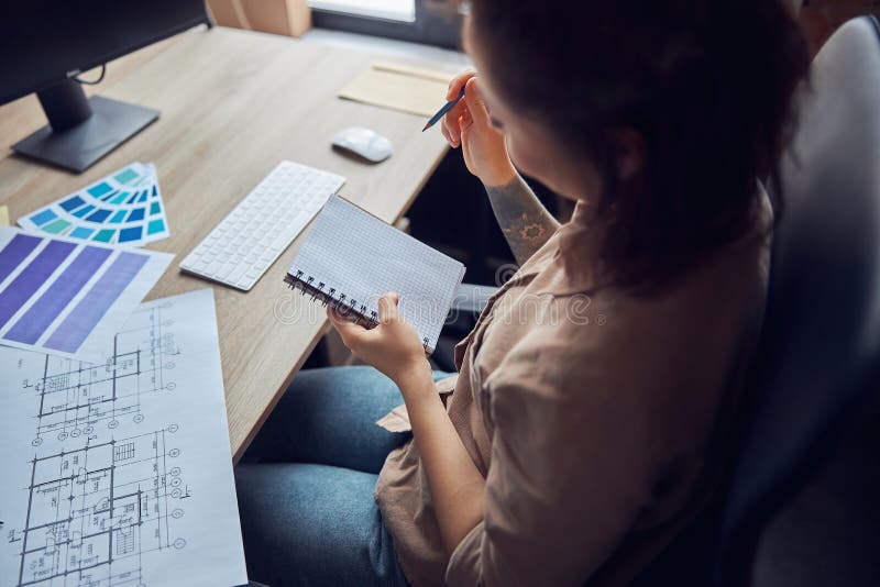 Female Interior Designer Holding Pencil, Making Notes in Her Notebook ...