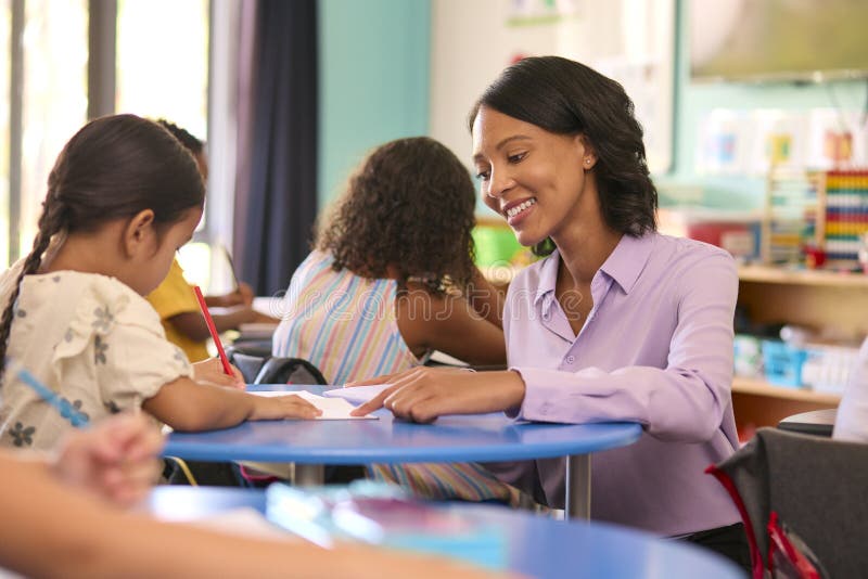 Female Primary or Elementary School Teacher Helping Students at Desks ...
